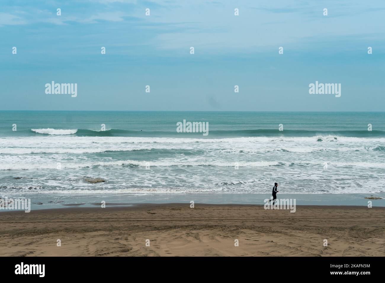 An aerial view of a man running along the coastline with foamy sea ...