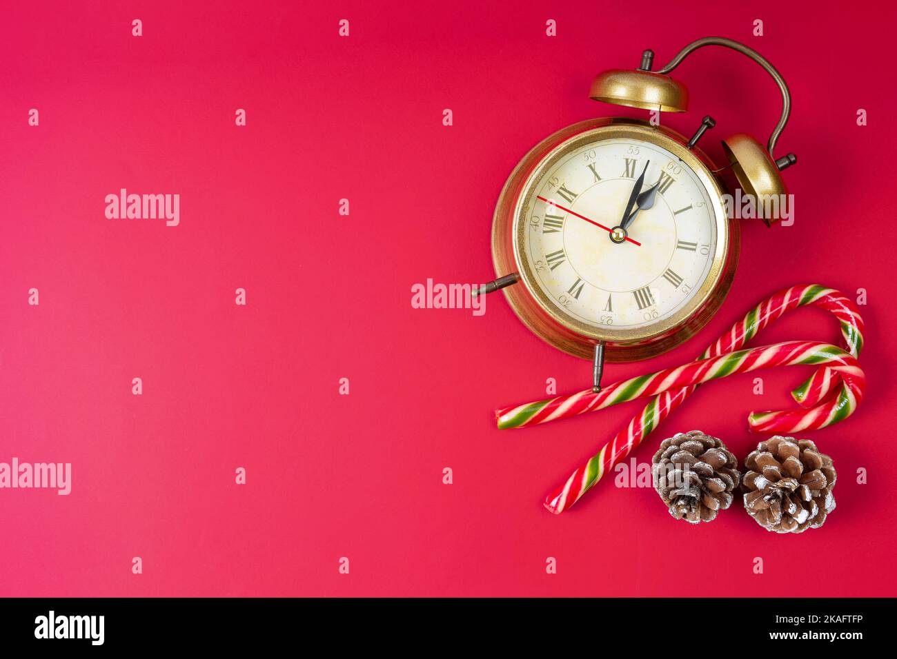 Bronze alarm clock, candy cane and fir cones on red background. Clock ...