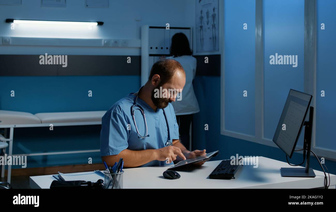 Practitioner assistant sitting at desk holding tablet computer ...