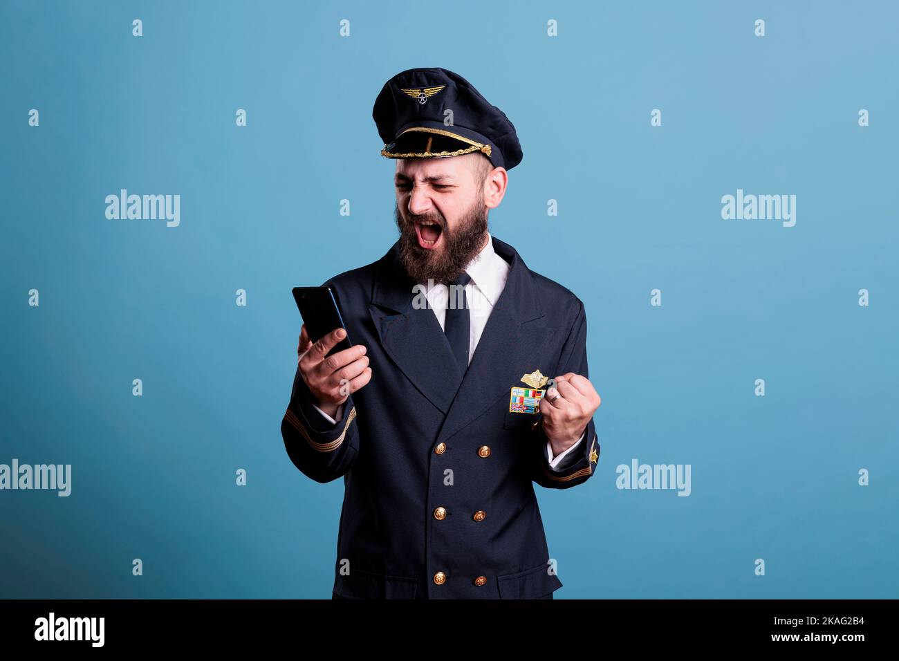 Happy smiling airplane pilot in uniform holding modern phone with ...