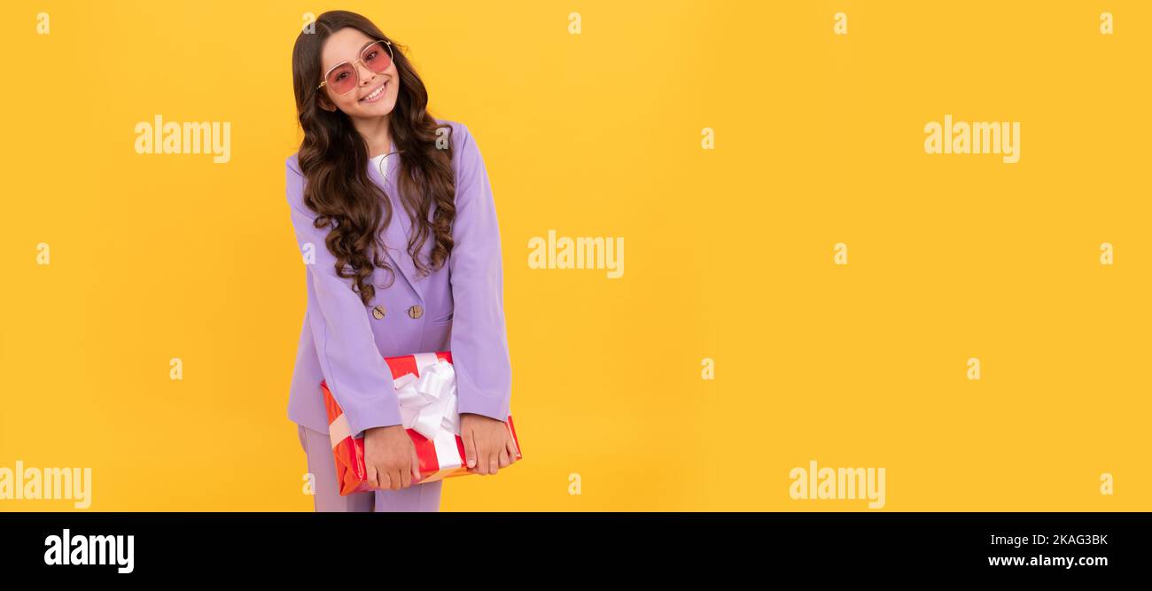 trendy cheerful child in sunglasses and suit hold present box on yellow ...