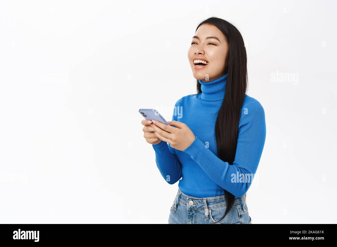 Laughing korean girl using mobile phone, smiling, holding smartphone ...