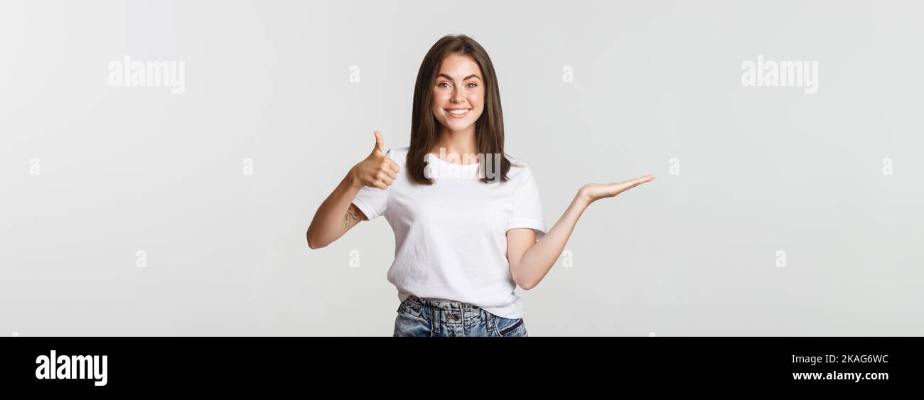 Satisfied attractive girl holding something on hand and showing thumbs ...