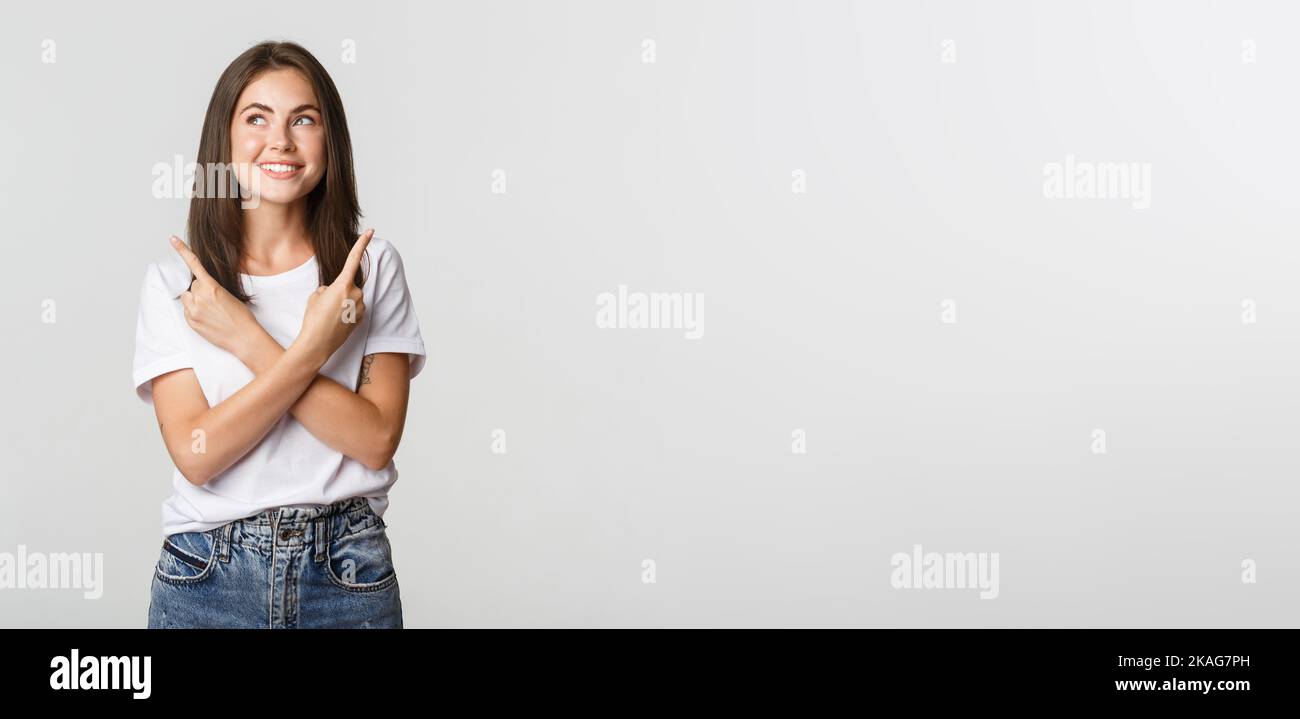 Thoughtful smiling woman looking upper left corner pleased, pointing ...