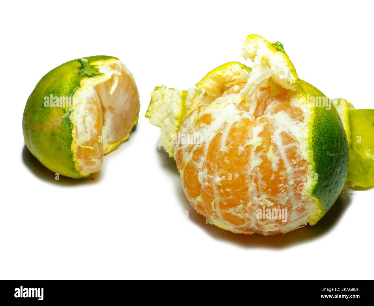 Unripe tangerine. Peeling a tangerine. Green fruit on a white ...