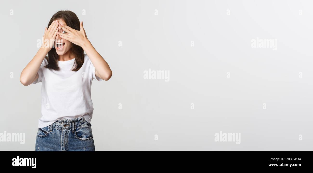 Excited and curious girl shut eyes and peeking through fingers amused ...