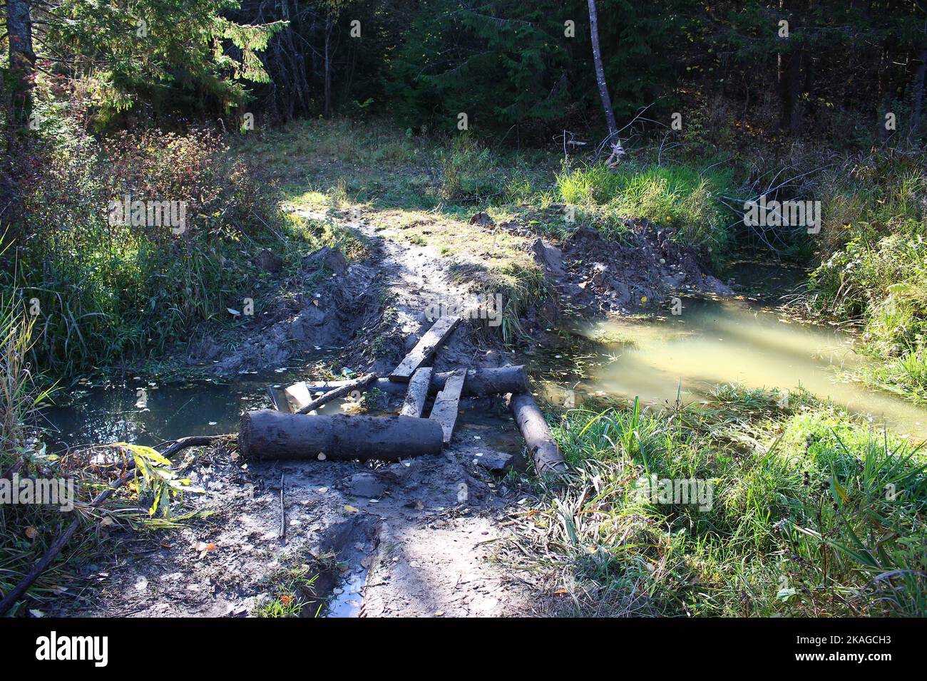 Broken small bridge over a muddy stretch of road with a large puddle ...