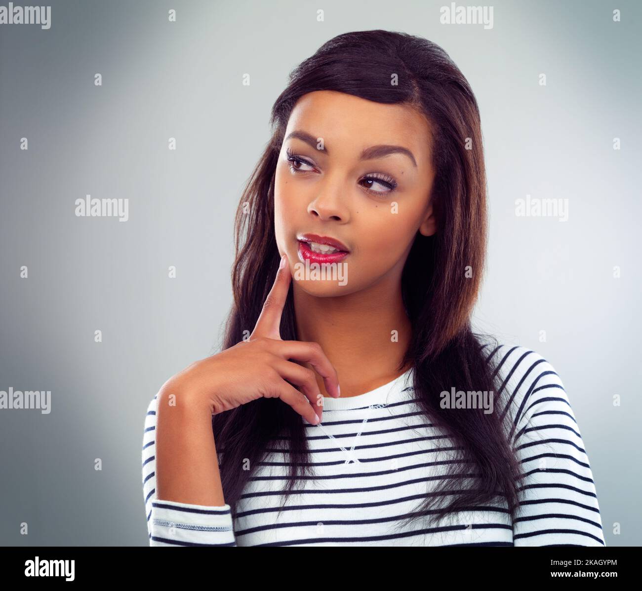 Thinking about her next pose. a young woman posing against a grey ...