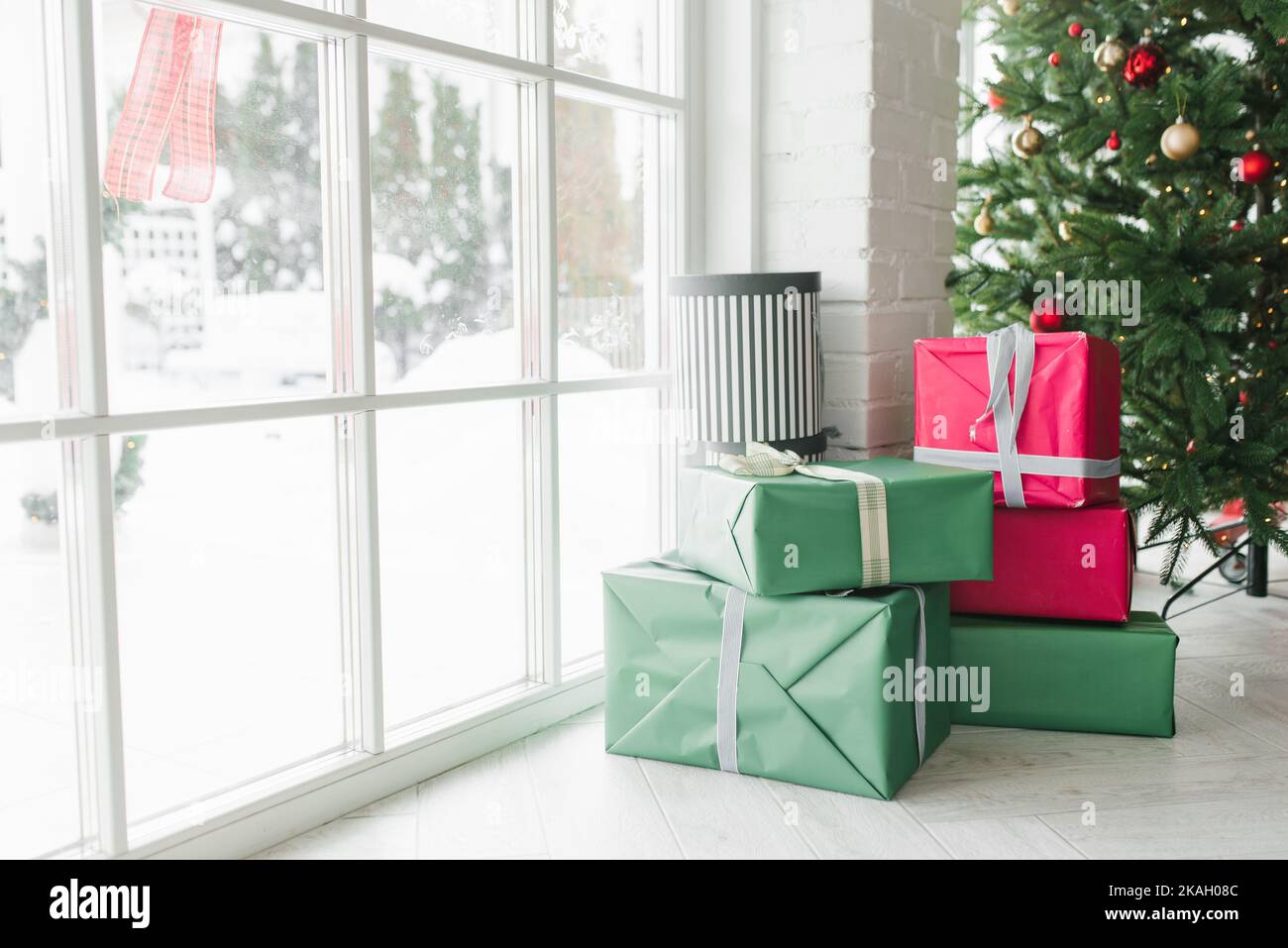 Gift boxes under the Christmas tree near the window in a cozy house ...