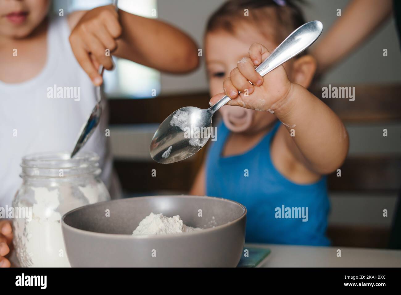 Close-up view of children's hands holding a spoon and adding flour to ...