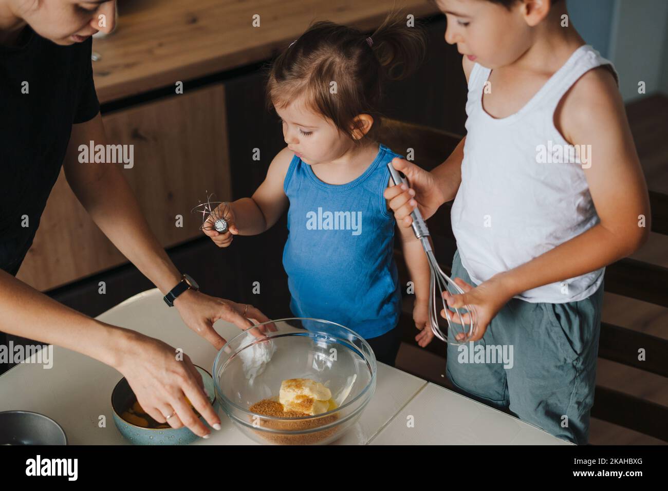 Adult woman and two cute kids adding ingredients into bowl with dough ...