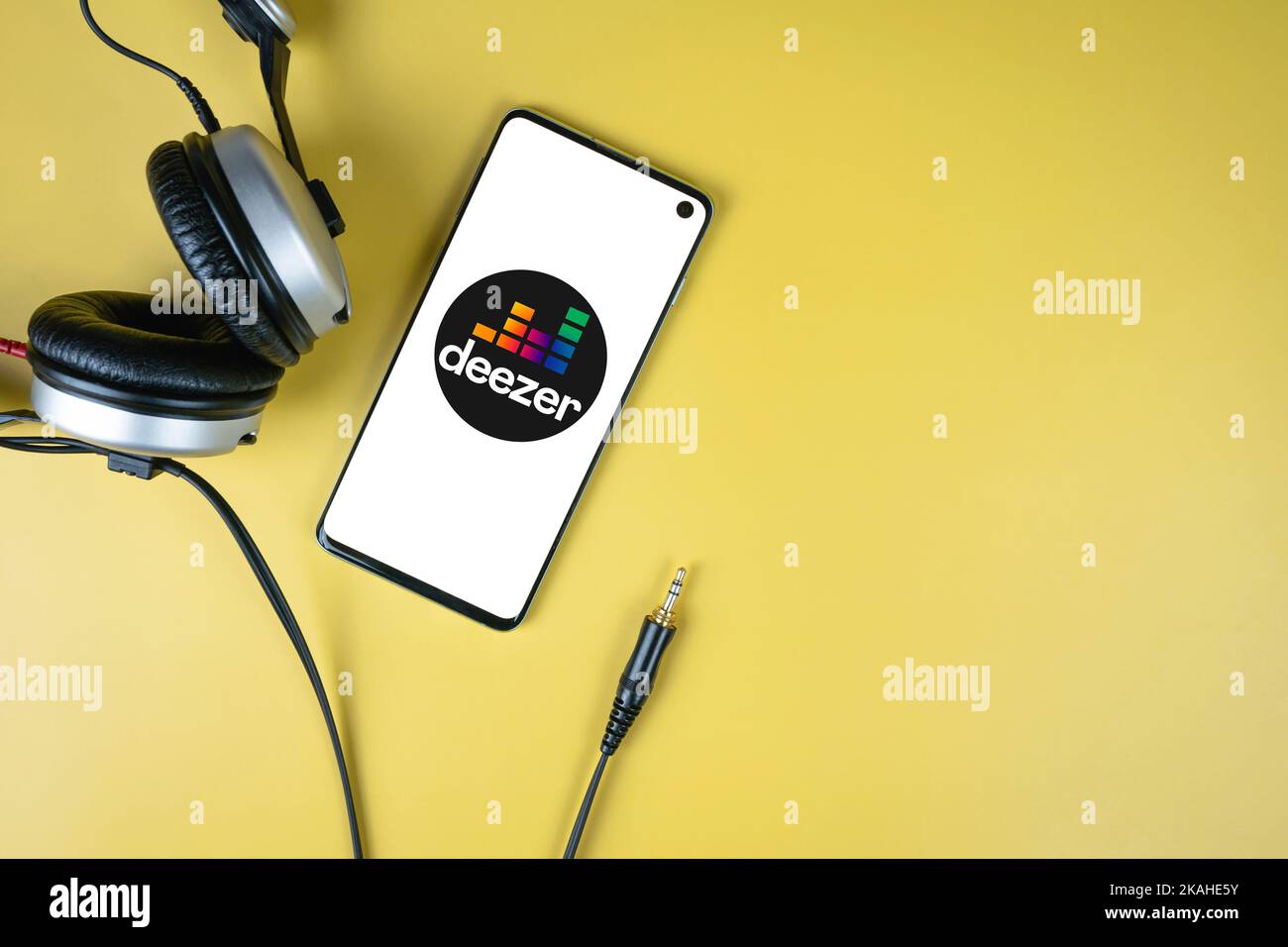 Deezer app logo on smartphone screen and headphones with jack on yellow ...