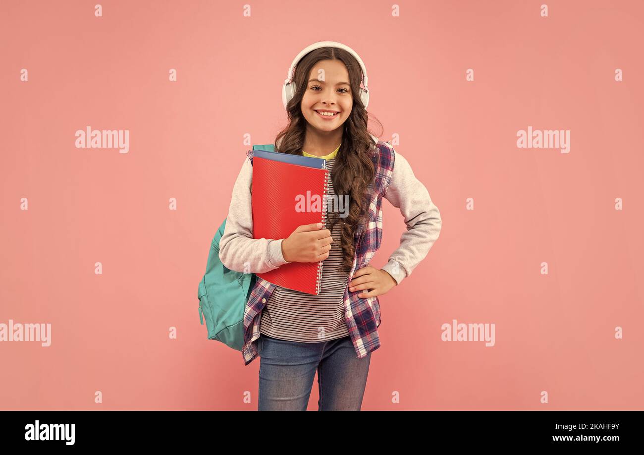 positive kid listening music in earphones with school bag and workbook ...