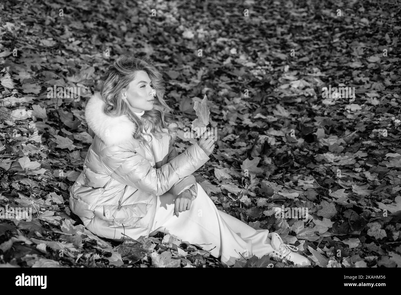 Get ready for the cold weather. Beautiful girl sit on fallen leaves ...