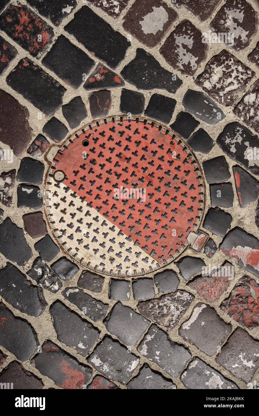an old metal sewer hatch painted red and white on a pedestrian crossing ...