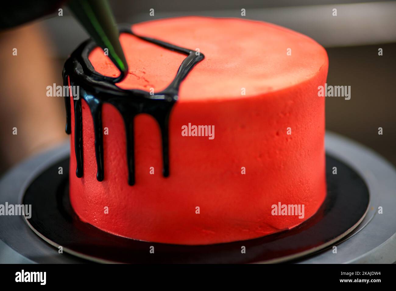 topping a red cake with black dark chocolate icing Stock Photo - Alamy