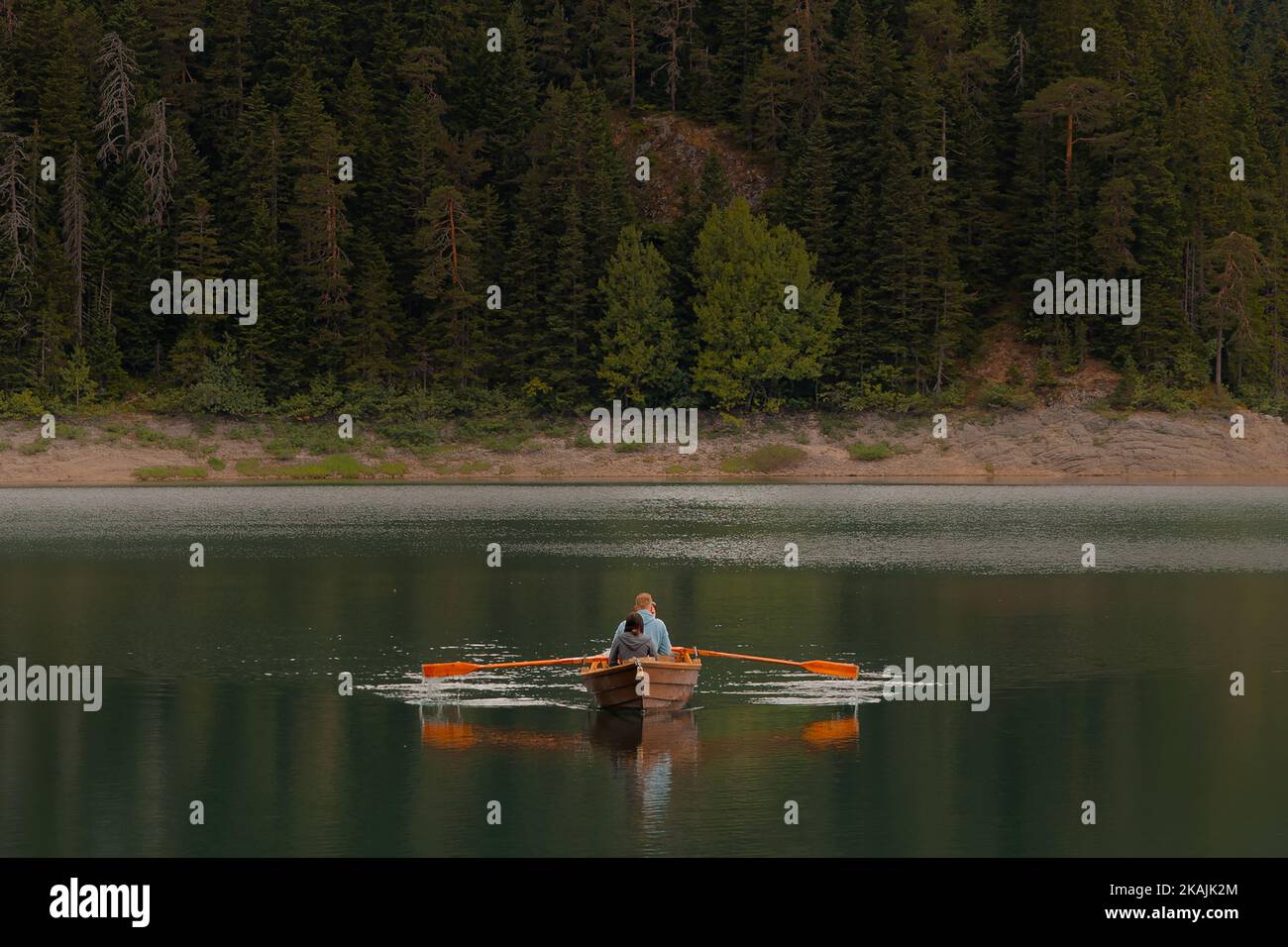 A back view of people rowing the boat in the middle of the lake in the ...