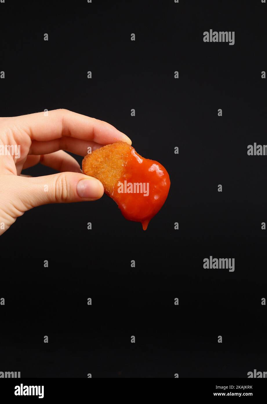 A hand holding a chicken nugget dipped in a tomato sauce isolated on ...