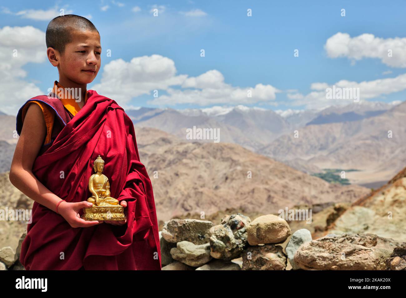 Young Buddhist monk holding a small golden Buddha statue at the Hemis ...