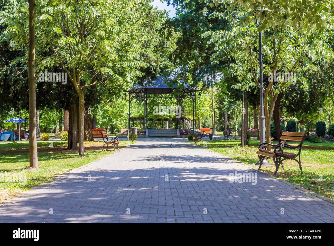 A park with a paved path leading to a gazebo surrounded by green trees ...