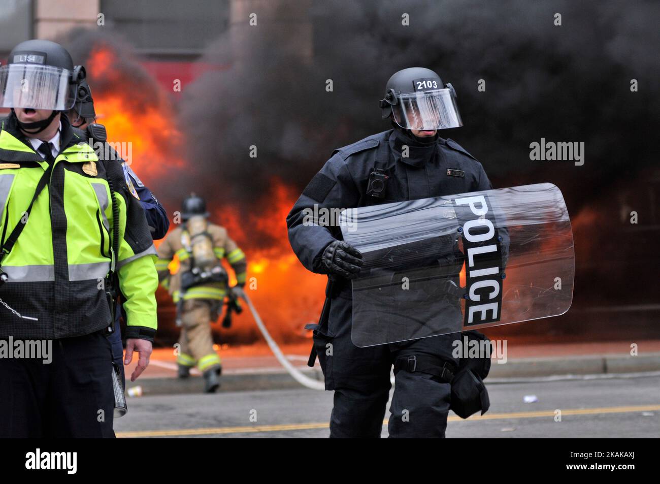 Protected by police officers in riot gear, firefighters battle a car ...