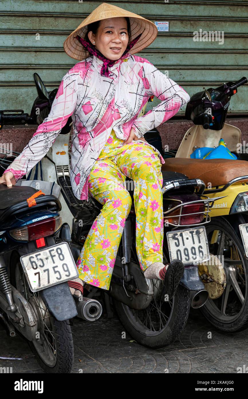 Vietnamese lady wearing bamboo hat sitting on parked motorcycle, Ho Chi ...