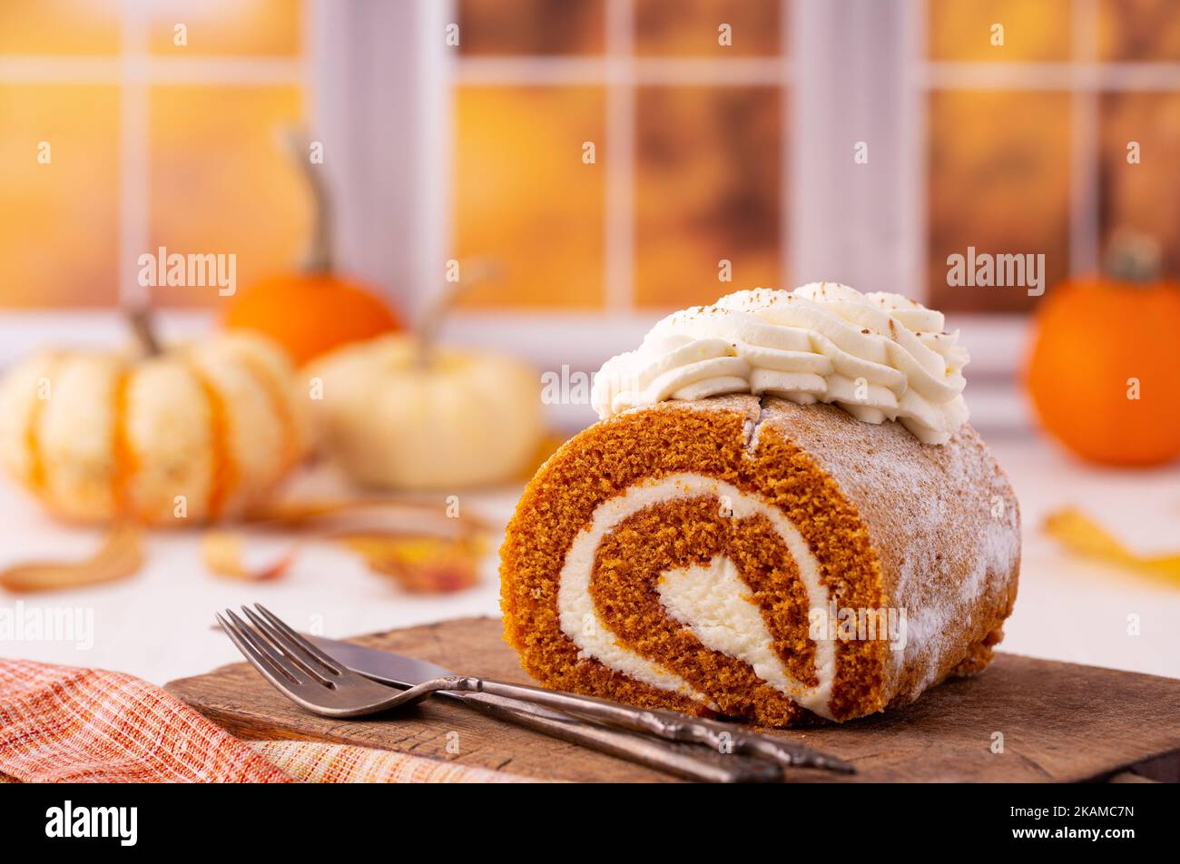 Baked pumpkin roll on a rustic cutting board with pumpkins out of focus ...
