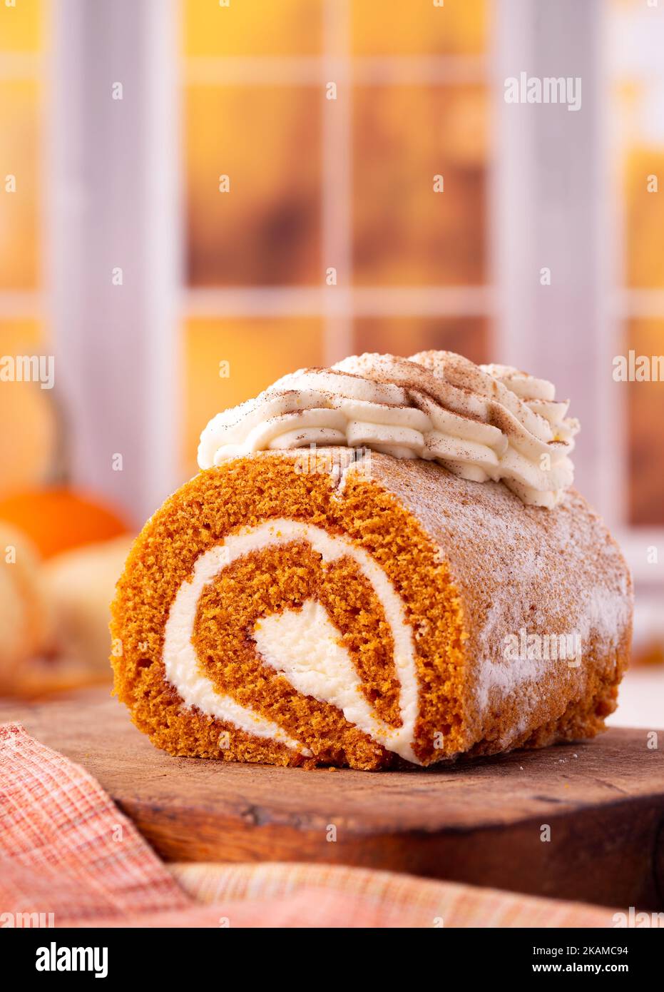 Baked pumpkin roll on a rustic cutting board with pumpkins out of focus ...