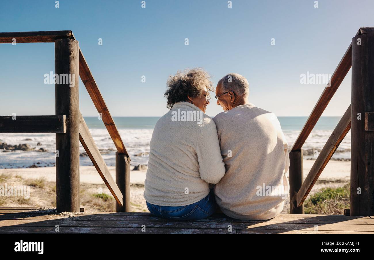 Happy senior couple smiling at each other while sitting on a wooden ...