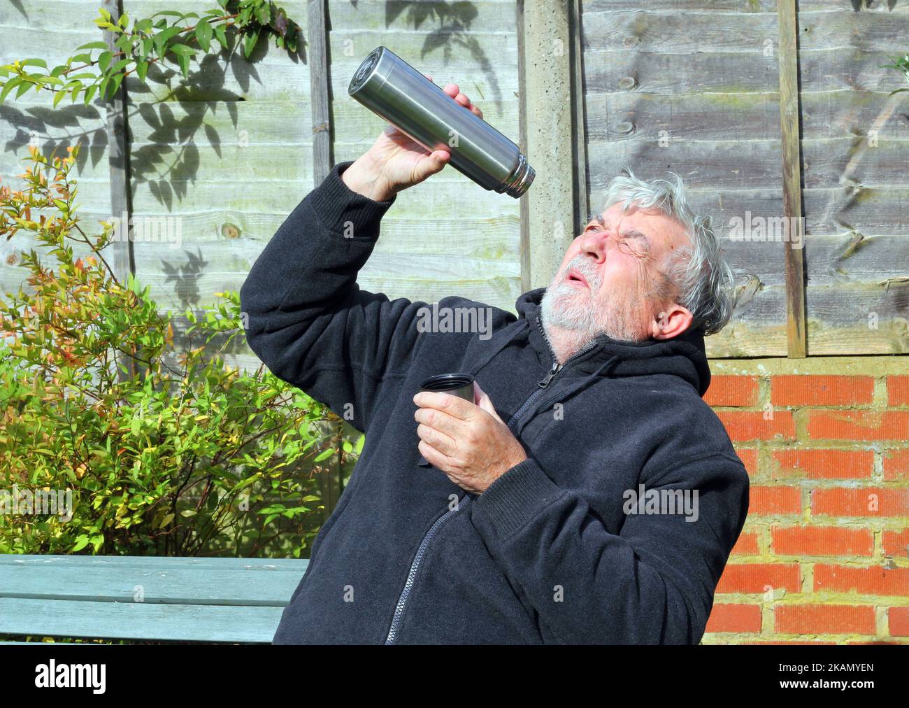 Senior or elderly man with a thermos flask which is empty. Drink has ...