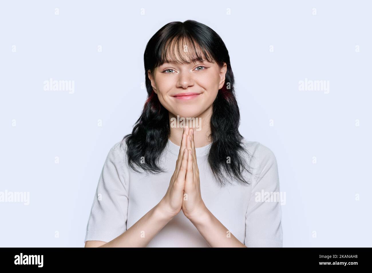 Young female pleading, holding hands in prayer on white background ...