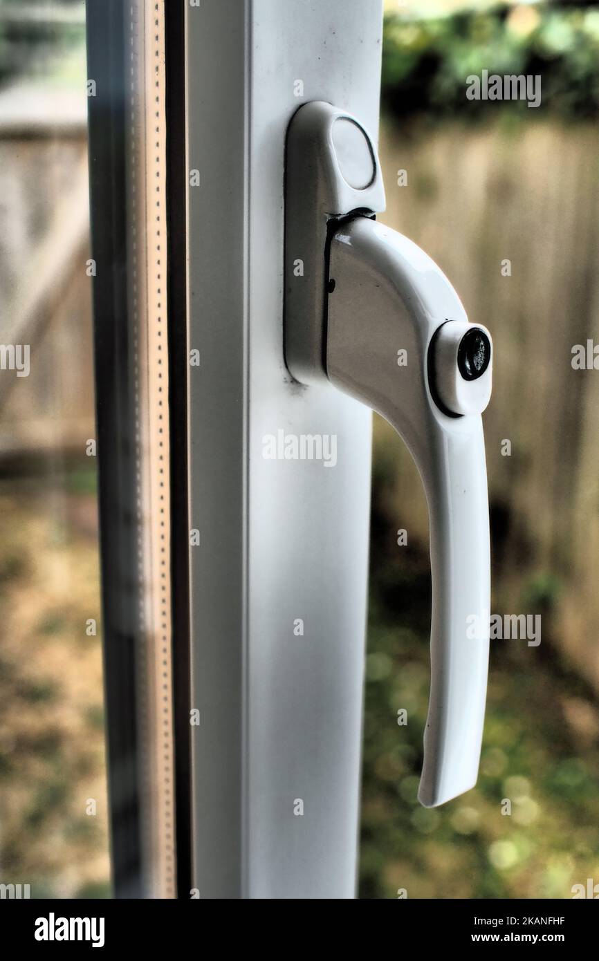 A vertical shot of a white window lock with a handle on a PVC window ...