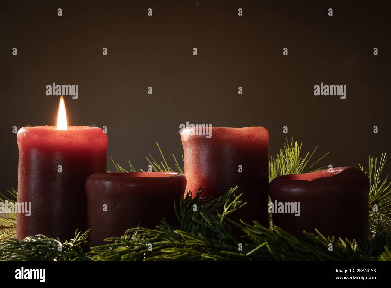 One red candle burning in an advent wreath with evergreen boughs and ...