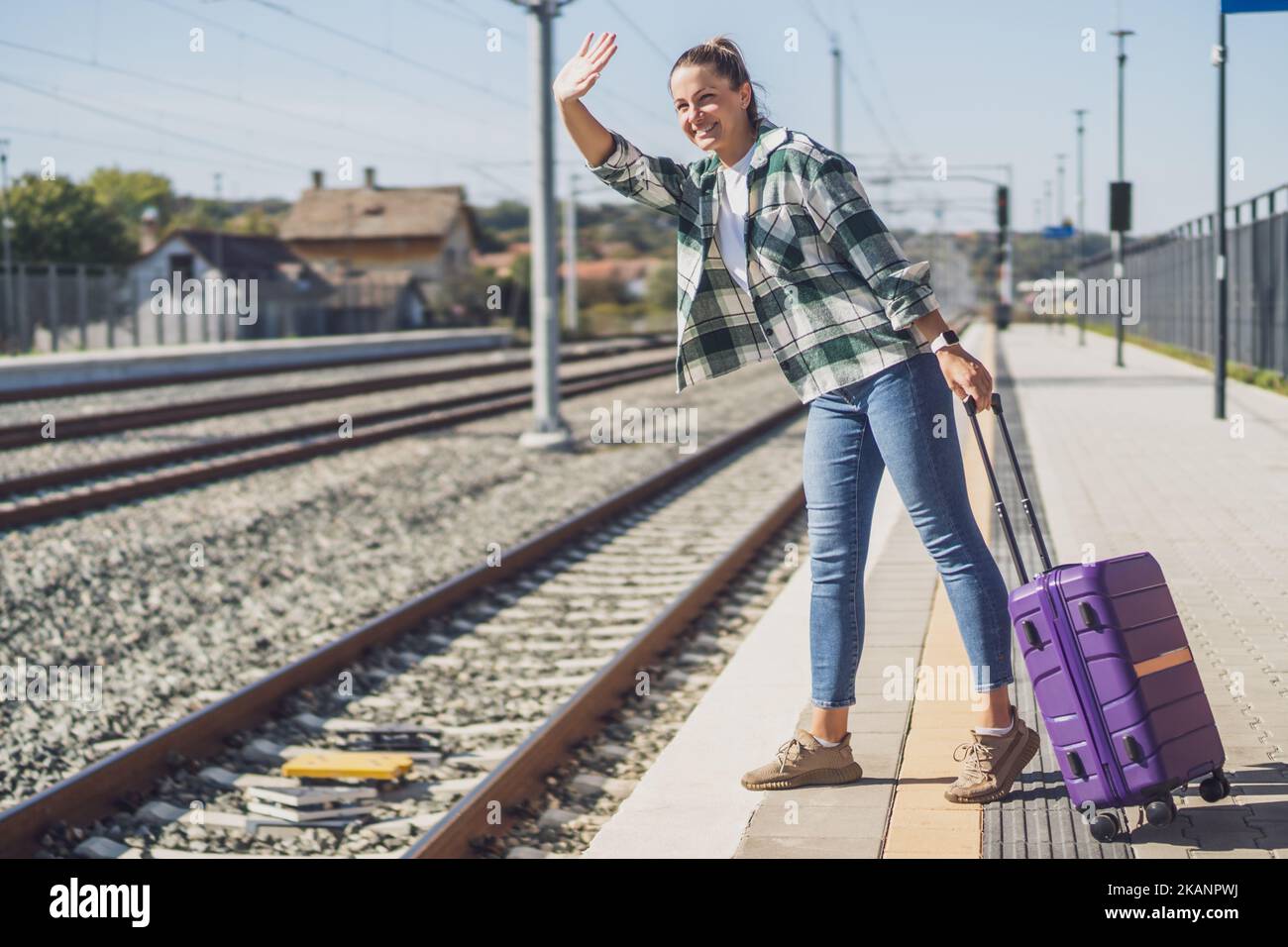 Happy woman with suitcase waving on a train station Stock Photo - Alamy
