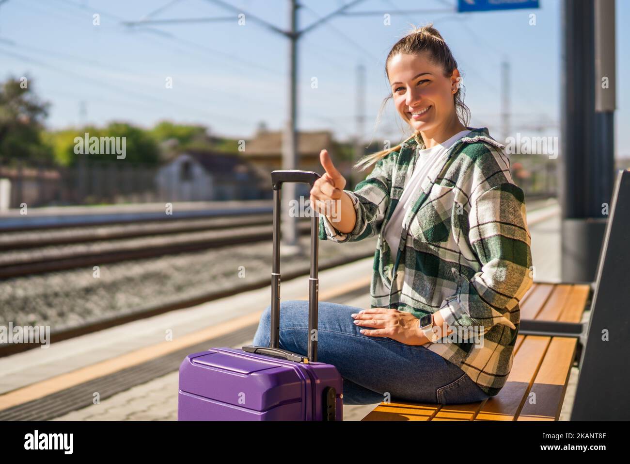Happy woman showing thumb up while sitting on a bench at the train ...