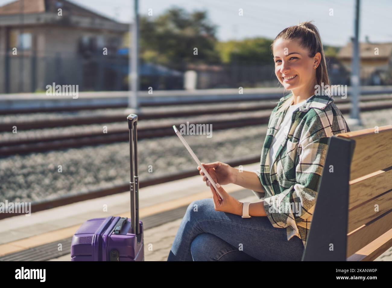 Happy woman using digital tablet while waiting for her train on a ...