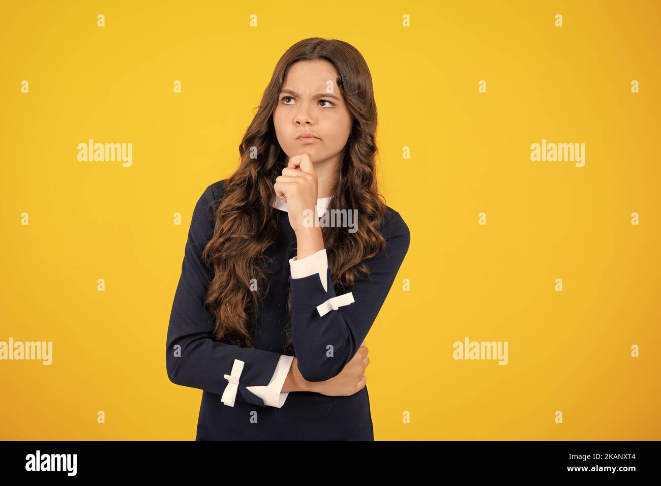 Smart nerdy school girl touching cheek and thinking against yellow ...