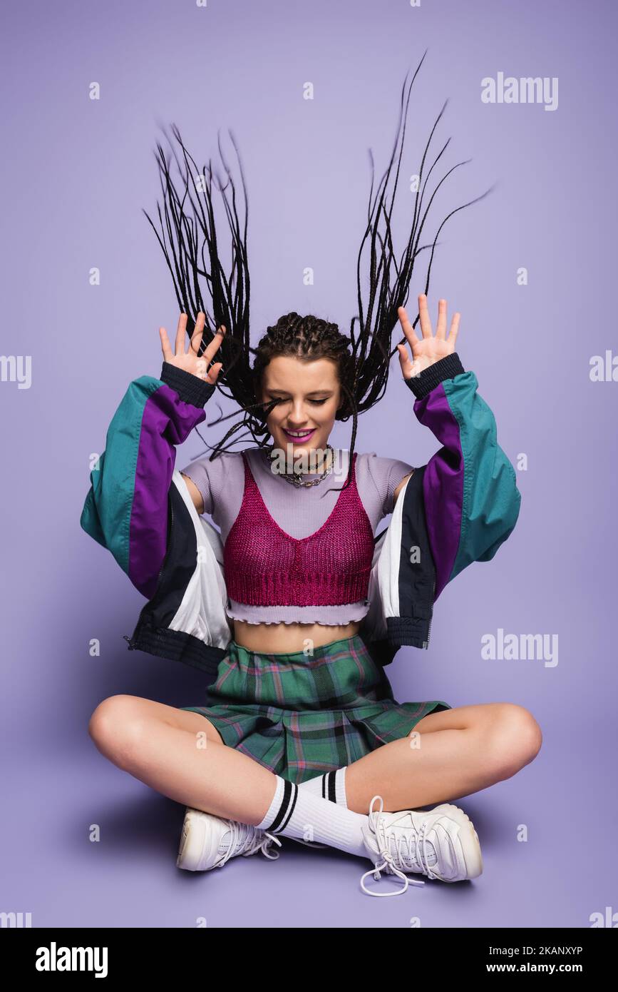 happy nineties style woman sitting with crossed legs on purple ...