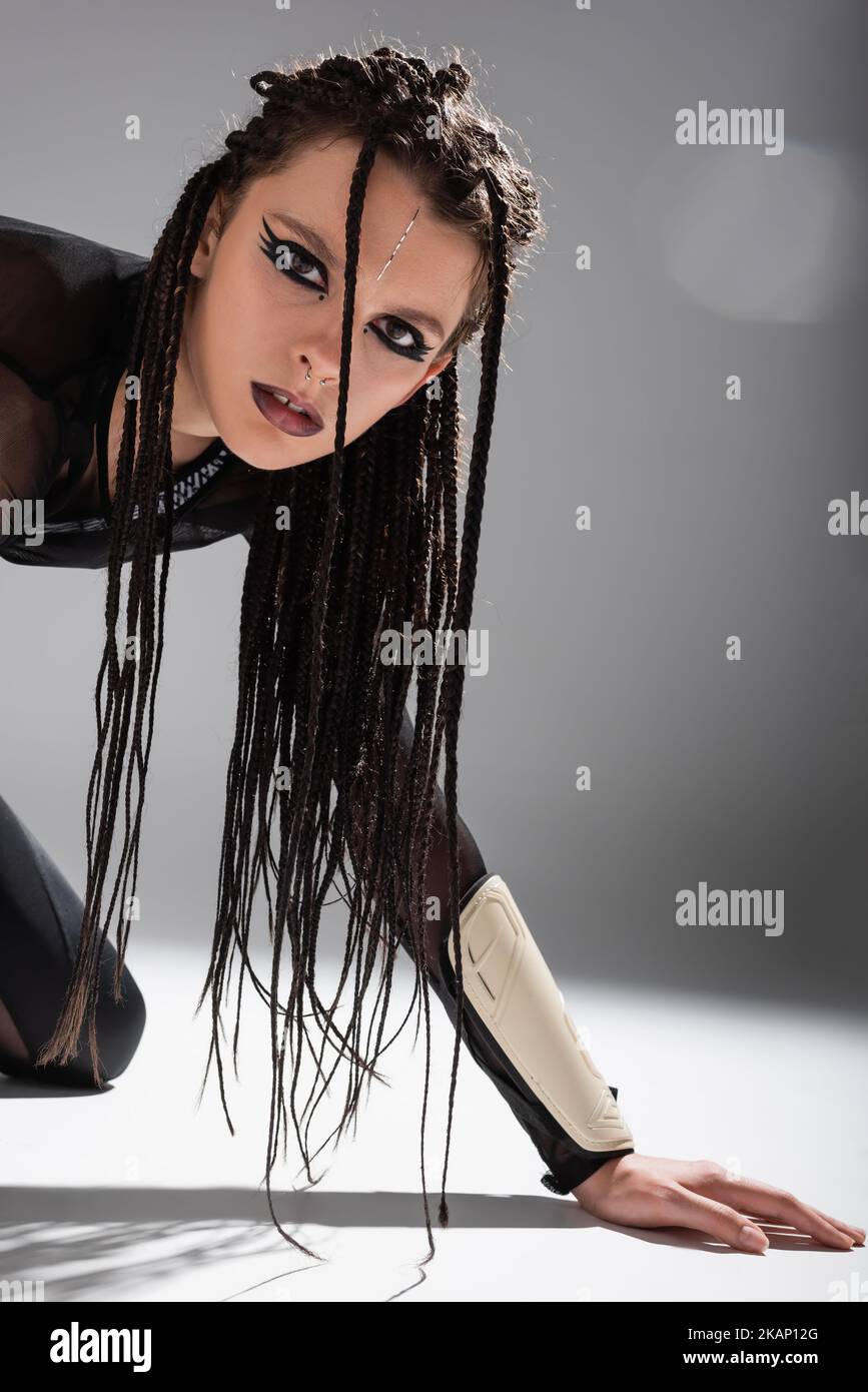 futuristic woman with stylish makeup and braided dreadlocks looking at ...