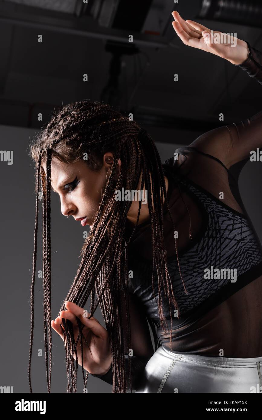 futuristic woman in black outfit touching braided dreadlocks while ...