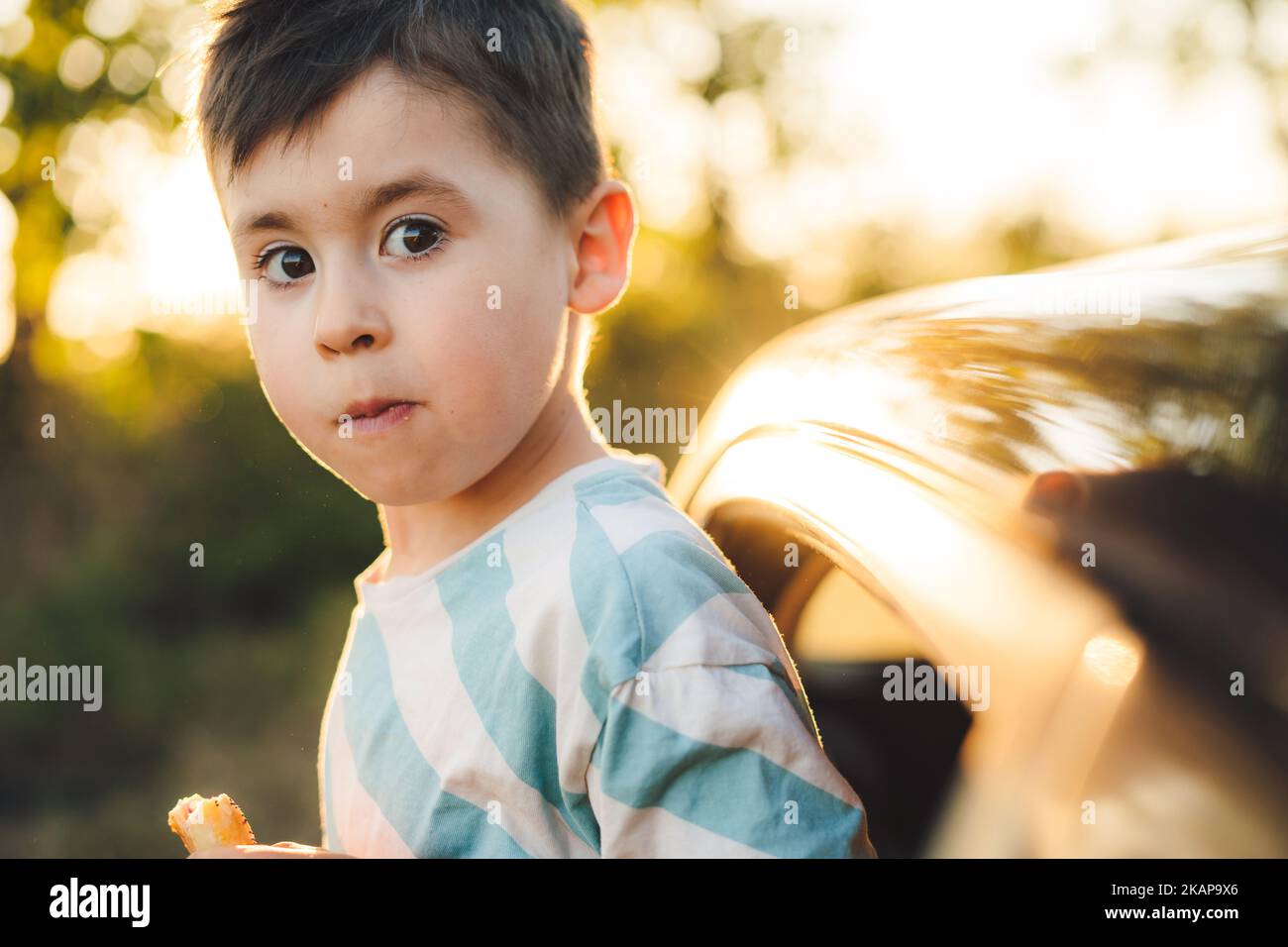 Boy is leaning out of the car window and enjoying snack on his road ...