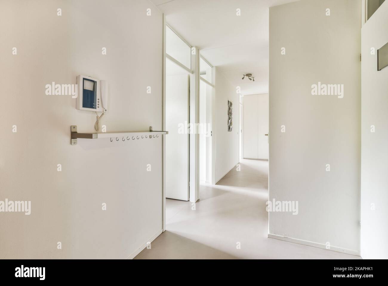 Narrow corridor with white walls and doors leading to spacious room ...