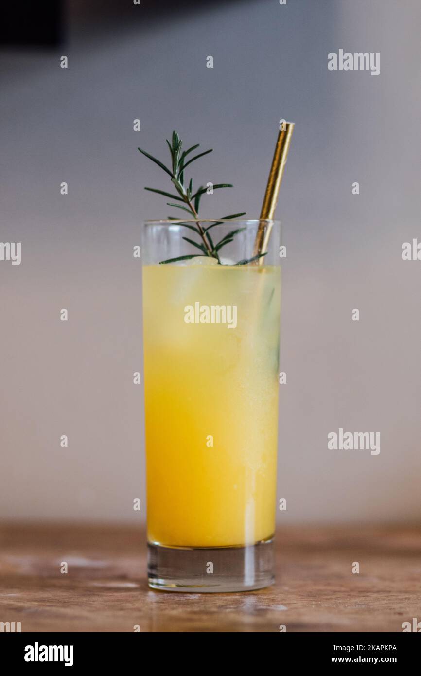 Orange cocktail in tall glass with rosemary garnish and a metal straw ...