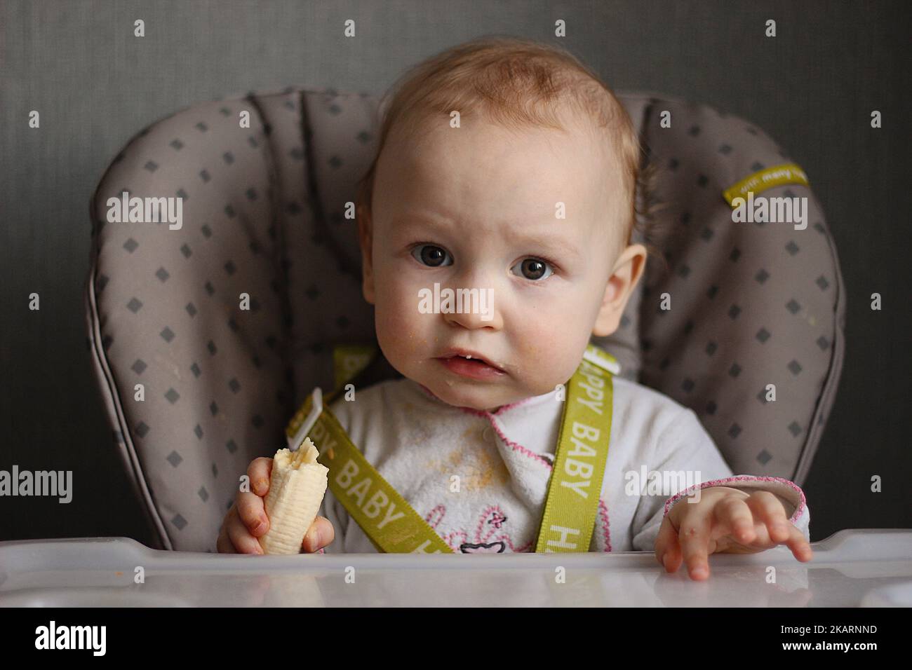 Baby boy holding banana in feeding chair Stock Photo - Alamy