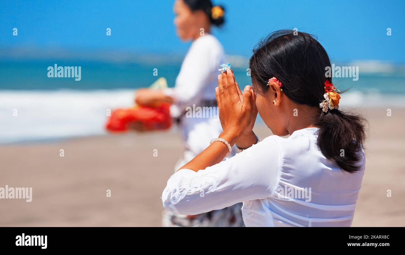Young balinese women praying with namaste hands on sea beach at ...