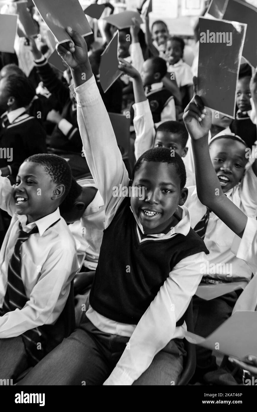 A grayscale shot of group of African children sitting in a row and ...