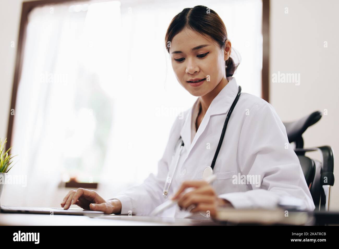 Portrait of an Asian female doctor using a computer and tablet to work ...