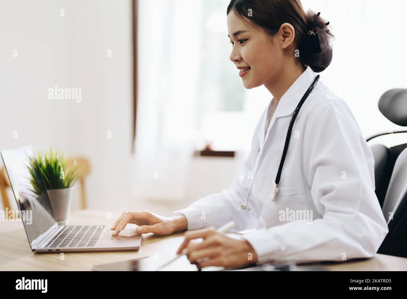 Portrait of an Asian female doctor using a computer and tablet to work ...