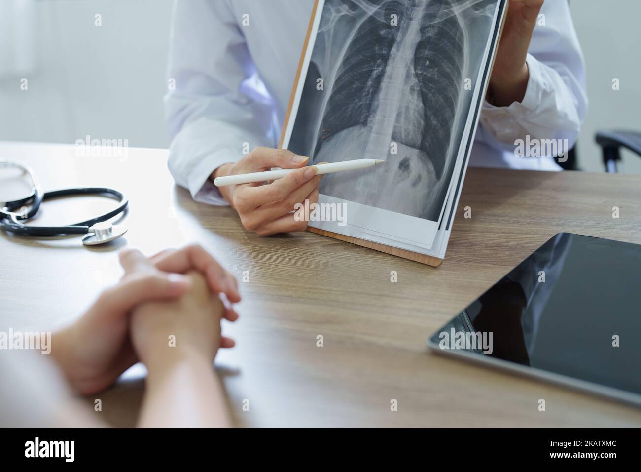 An Asian female doctor points to a patient x-ray film to explain the ...