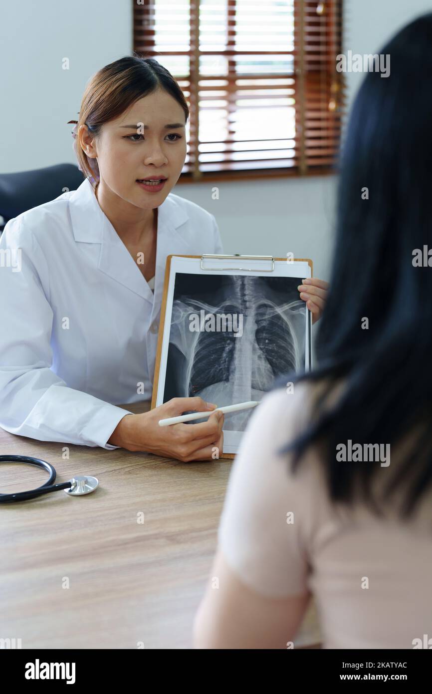 An Asian female doctor points to a patient x-ray film to explain the ...